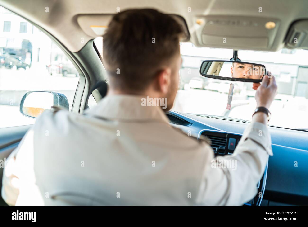Driver looks in the rearview mirror. Man adjusts the mirror in the car ...