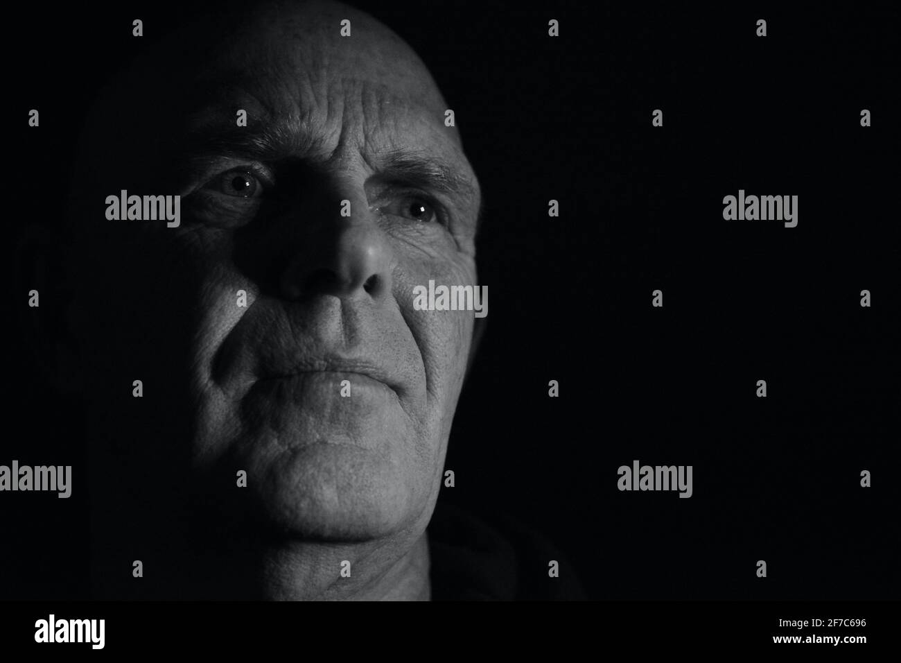 A monochrome headshot of mature male with a bald head and light shining ...