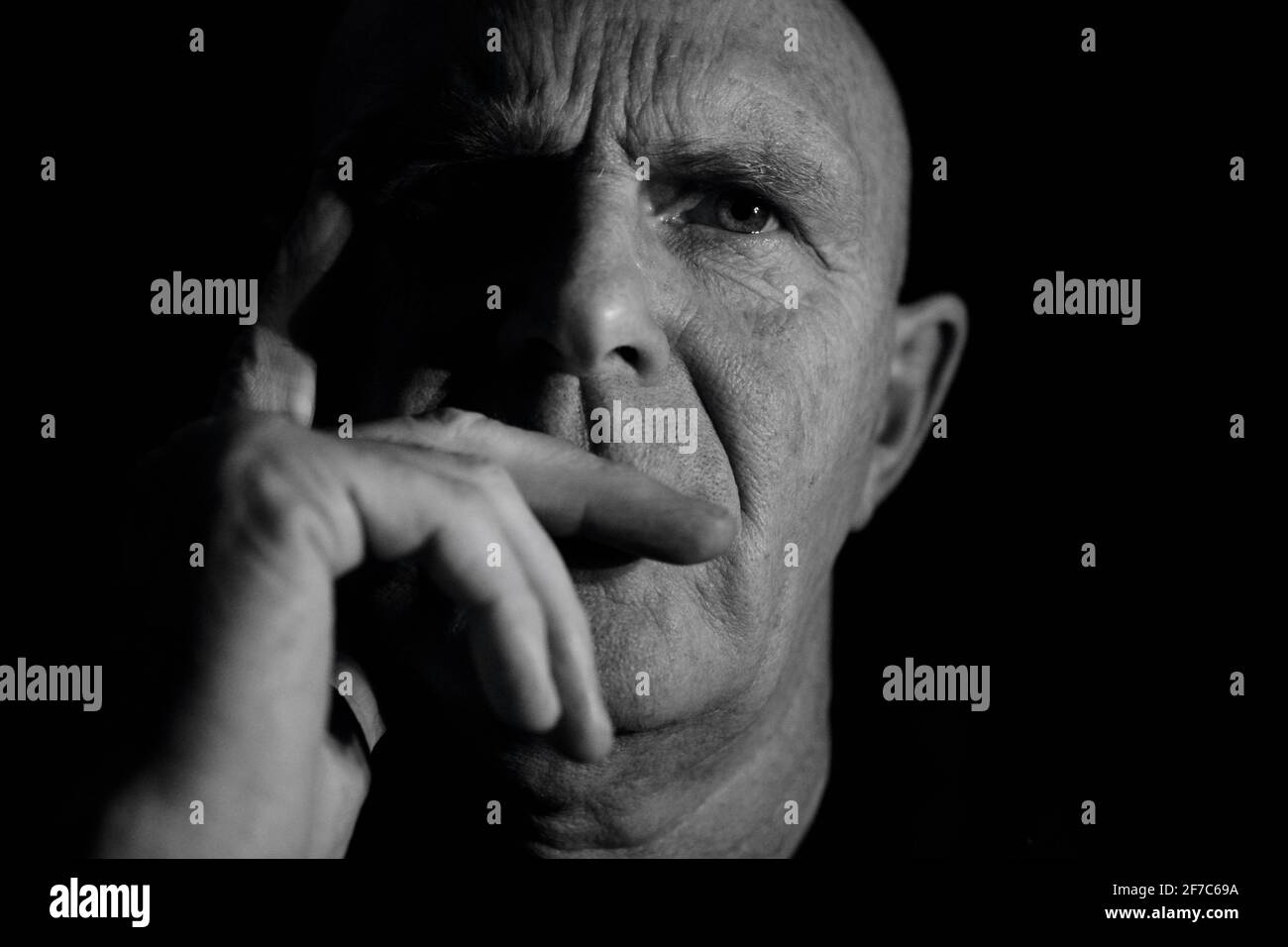 A monochrome headshot of mature male with a bald head and light shining ...