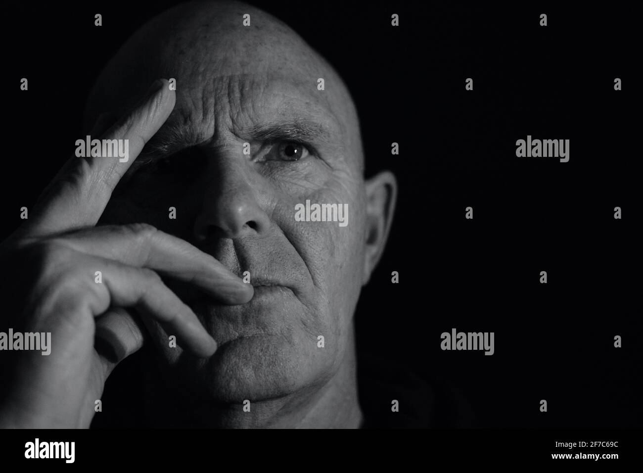 A monochrome headshot of mature male with a bald head and light shining ...