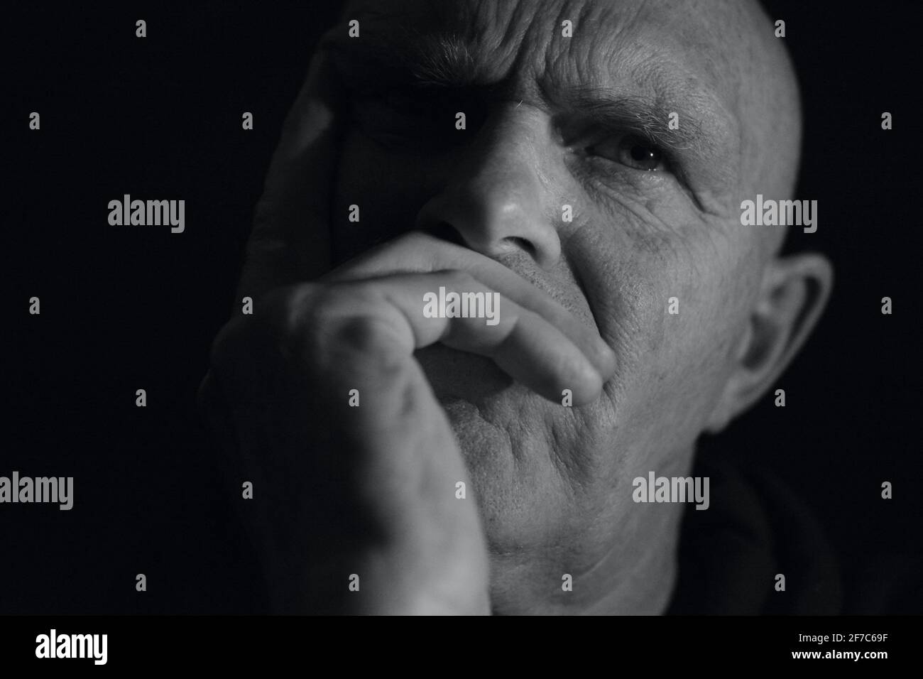 A monochrome headshot of mature male with a bald head and light shining ...