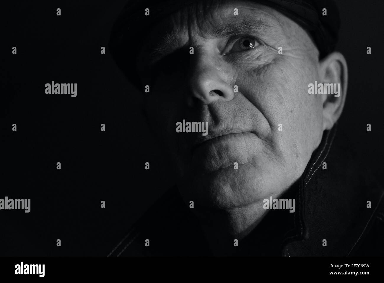 A monochrome headshot of mature male with a bald head and light shining ...