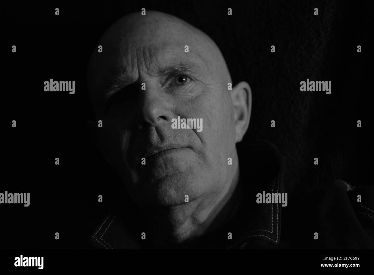 A monochrome headshot of mature male with a bald head and light shining ...