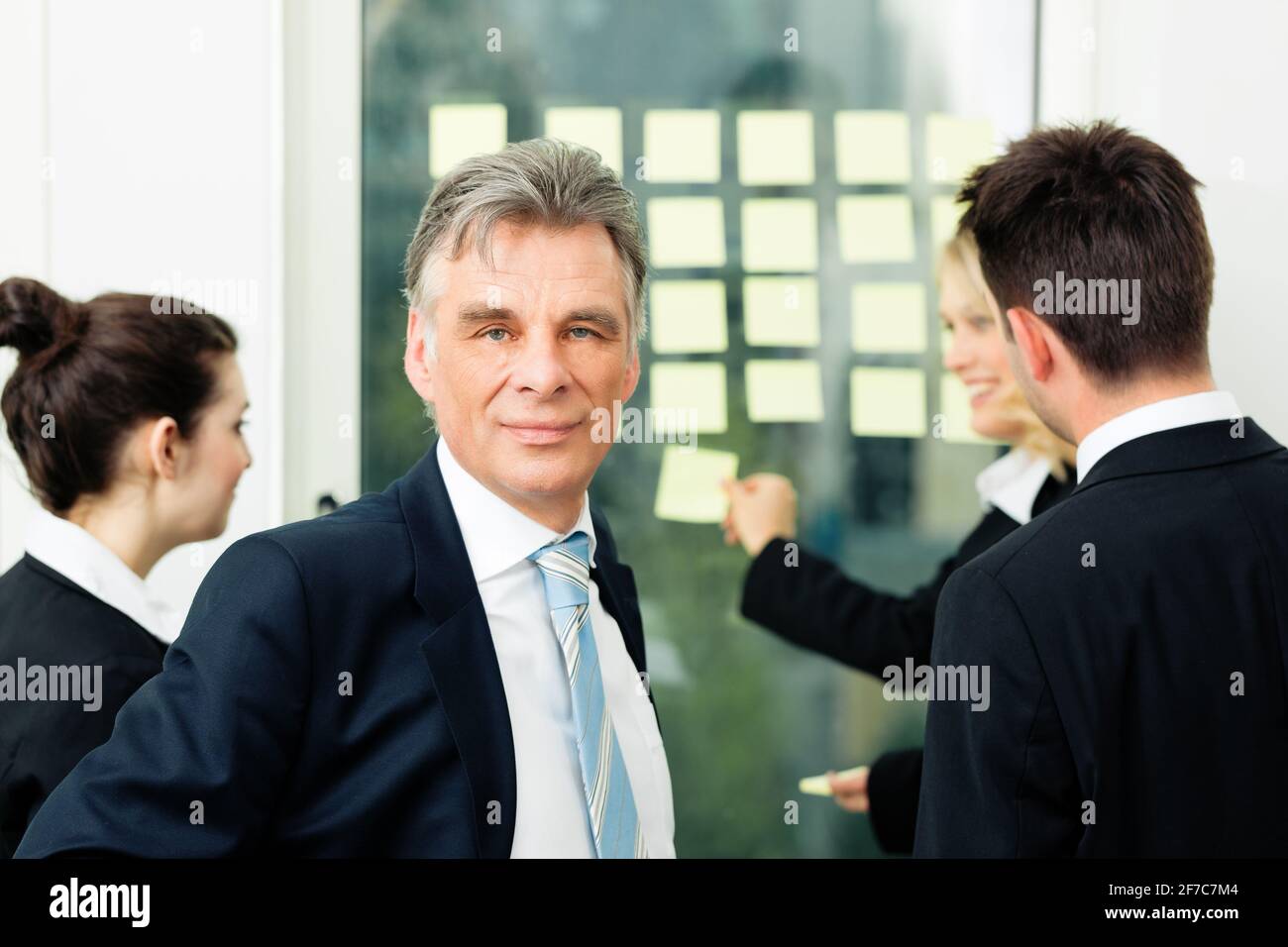 Business - team in an office; the senior executive is standing in front ...