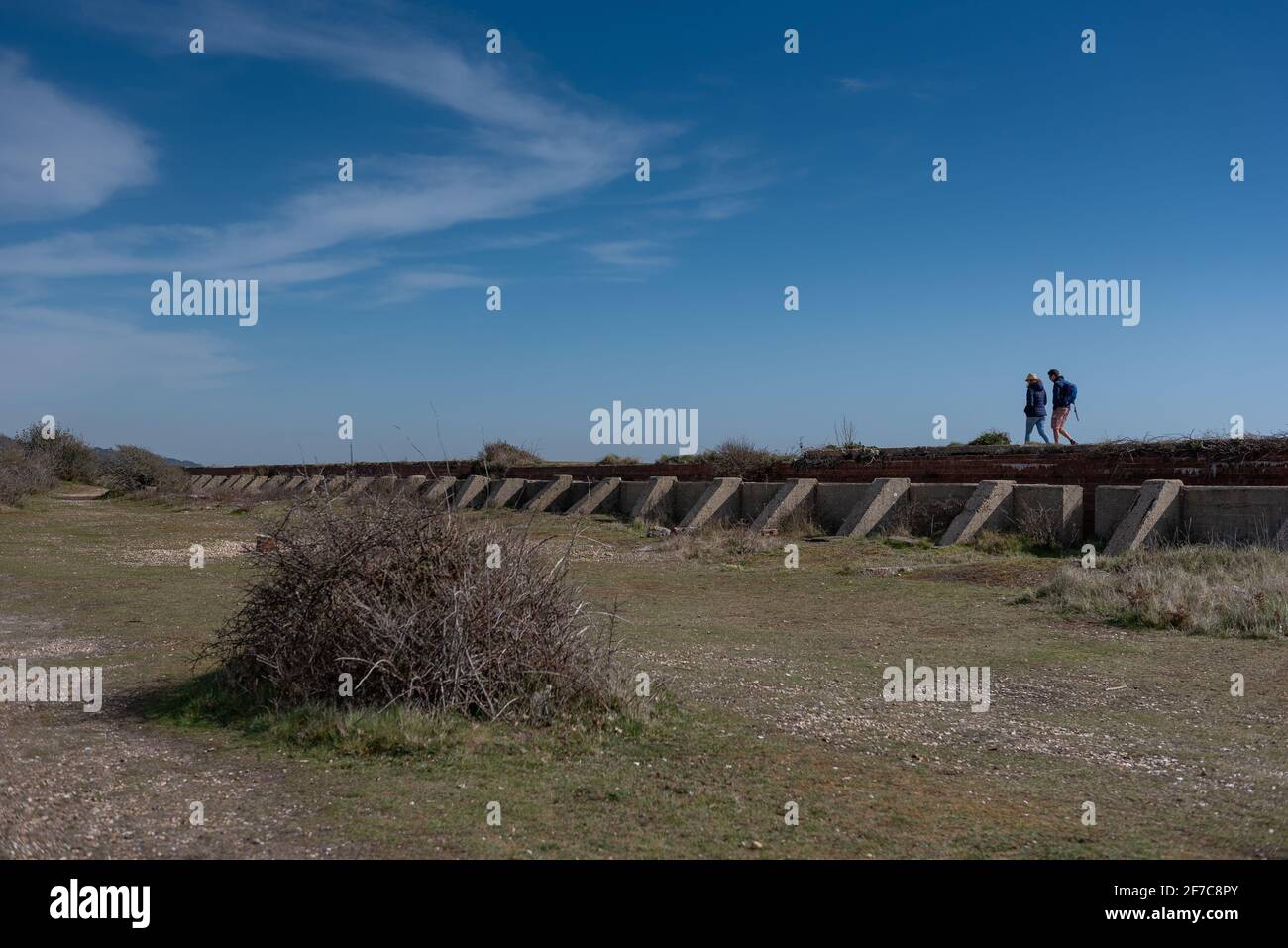 Two people walking along wall defence ww2 Lepe country park Stock Photo ...