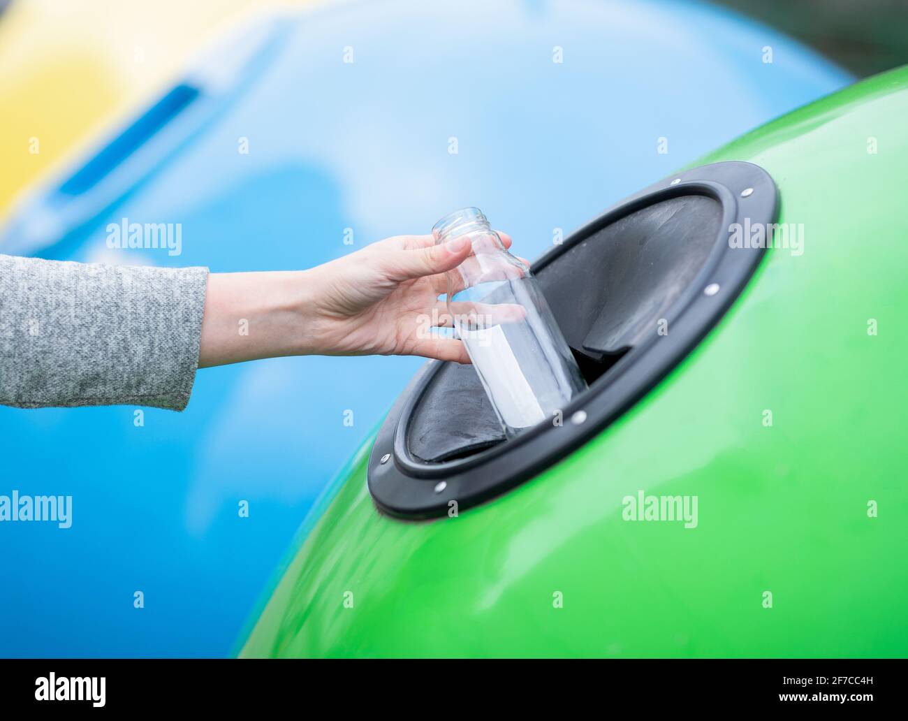 Female hand throwing empty glass bottle into yellow recycle bin container outdoors Stock Photo ...