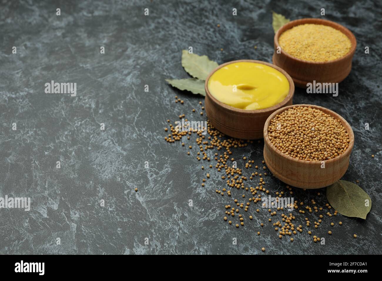 Bowls with mustard seeds, sauce and powder on black smoky background ...