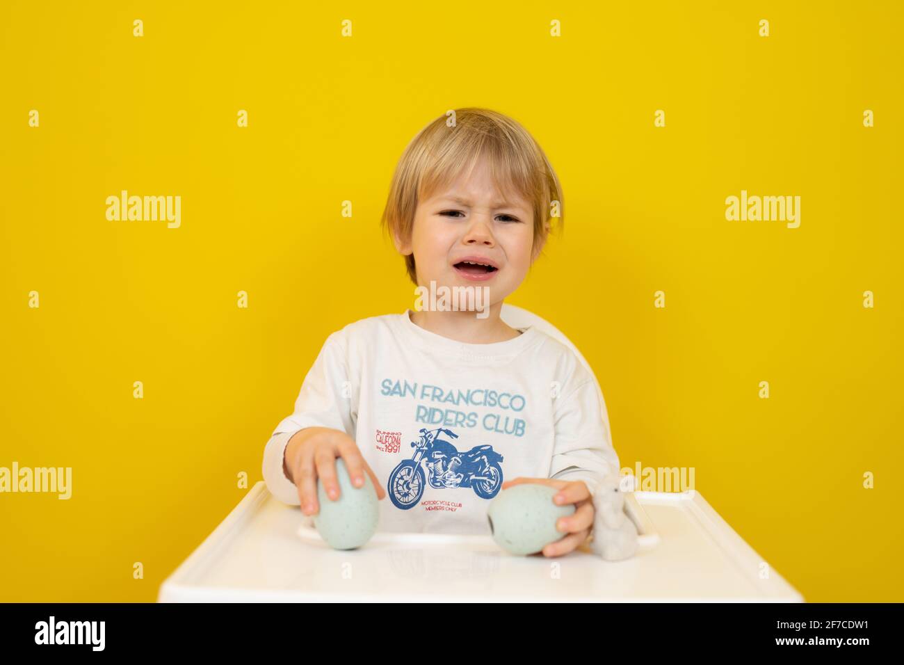 Beautiful baby boy sitting and crying while holding two easter eggs ...