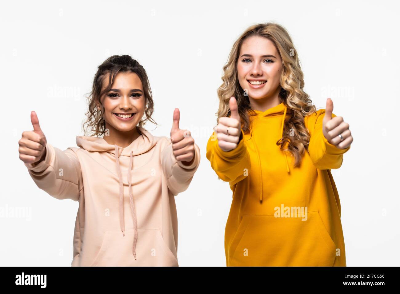 Two beautiful young women giving victory hand sign isolated on white ...