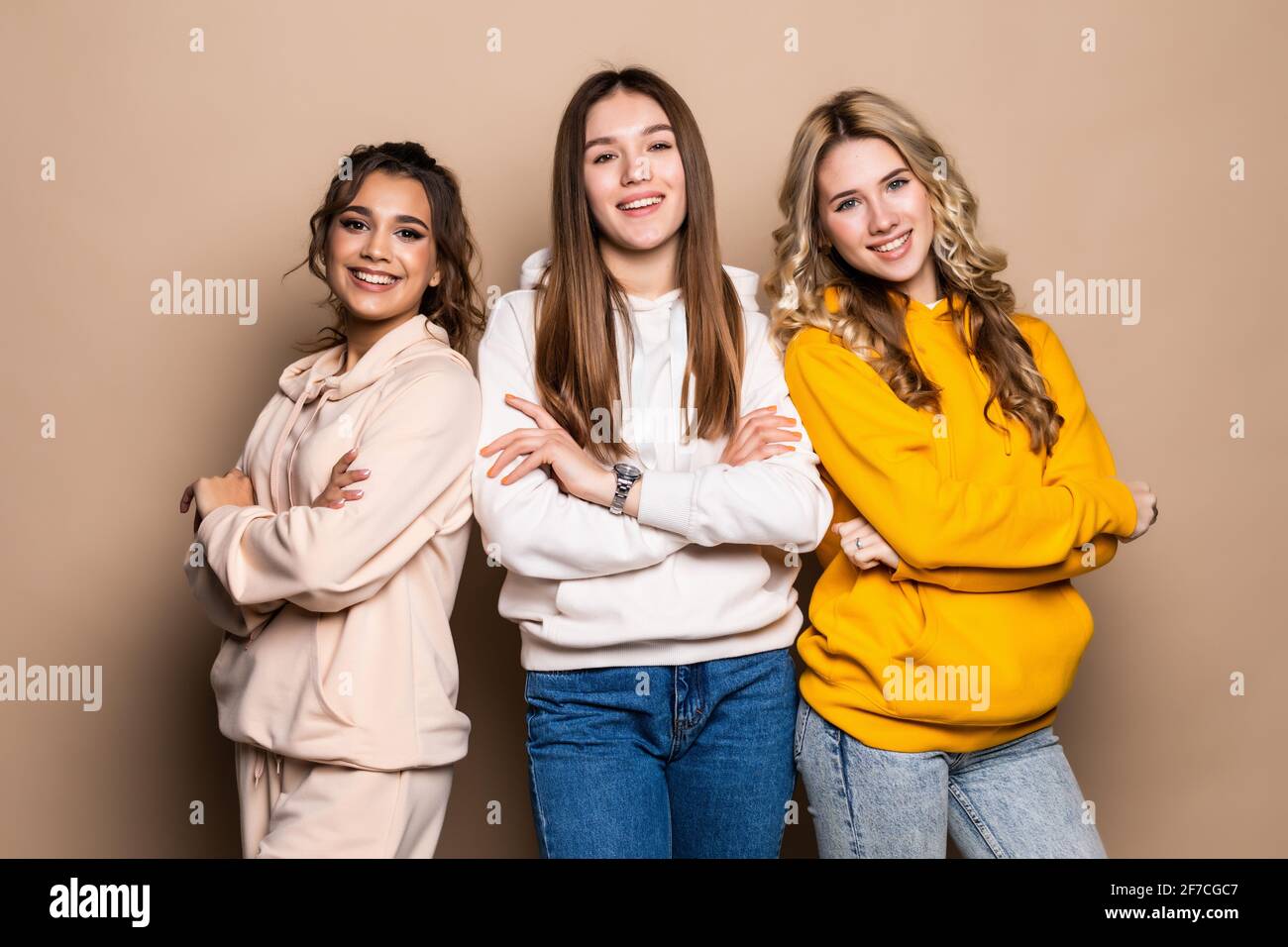 Three women friends standing together on beige background Stock Photo ...