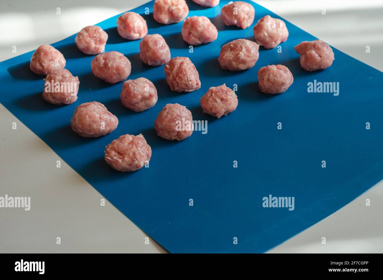 Raw shaped meatballs on blue. Rows of meatballs with pepper, salt and ...