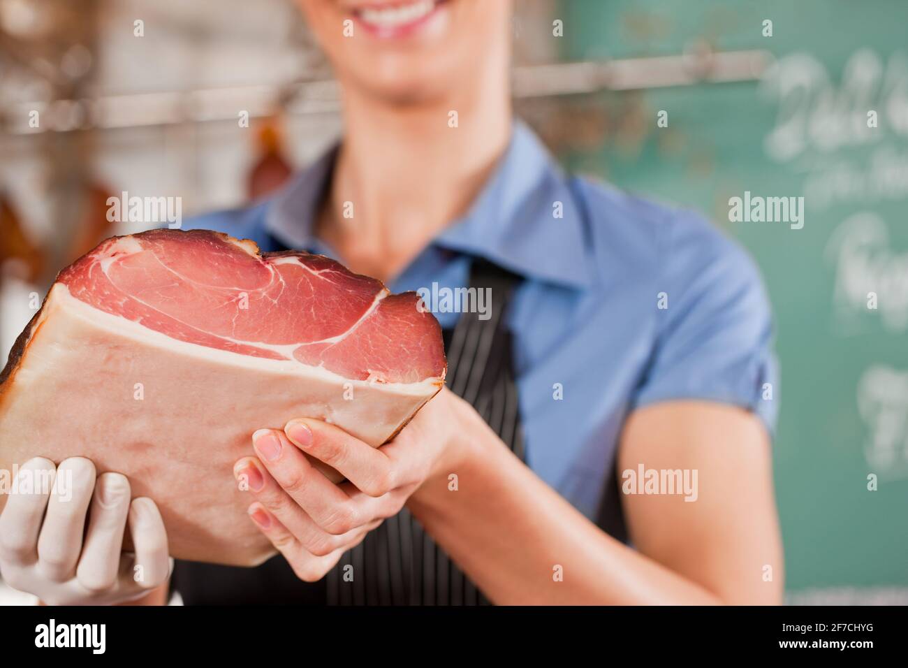Young woman or female butcher with raw ham in butchers shop; she is ...