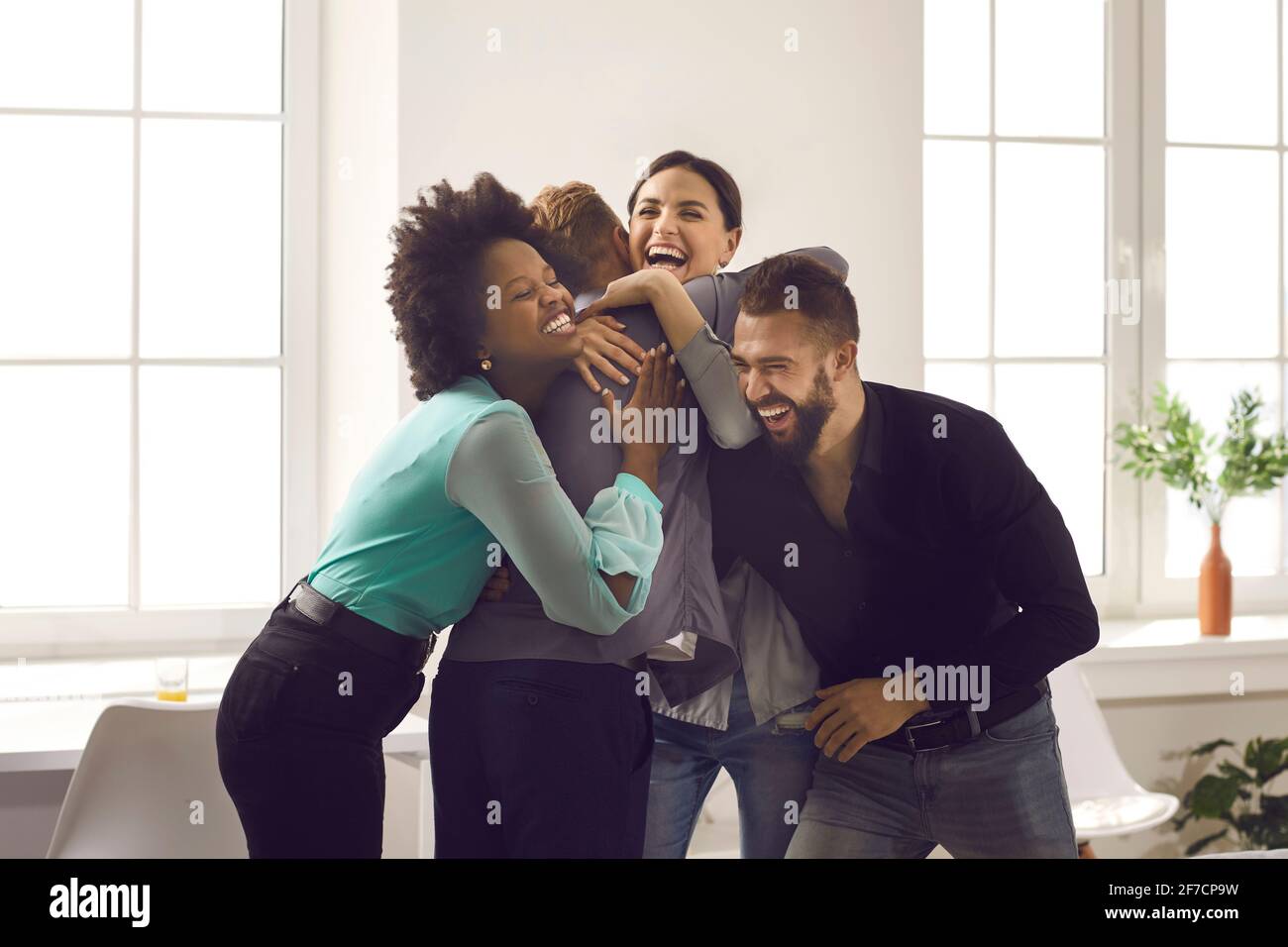 Group of young people hugging friend congratulating him on promotion or ...