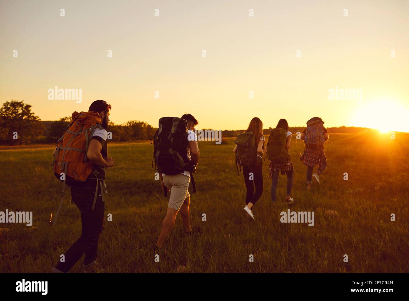 Group of five people with large backpacks move in a row across a field ...