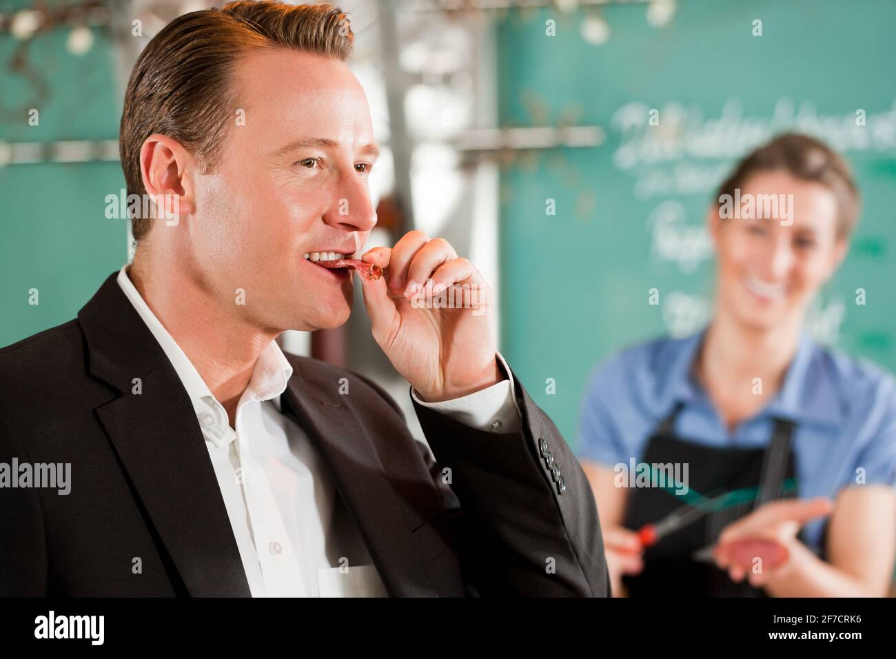 Customer eating fresh meat with female butcher in background Stock ...