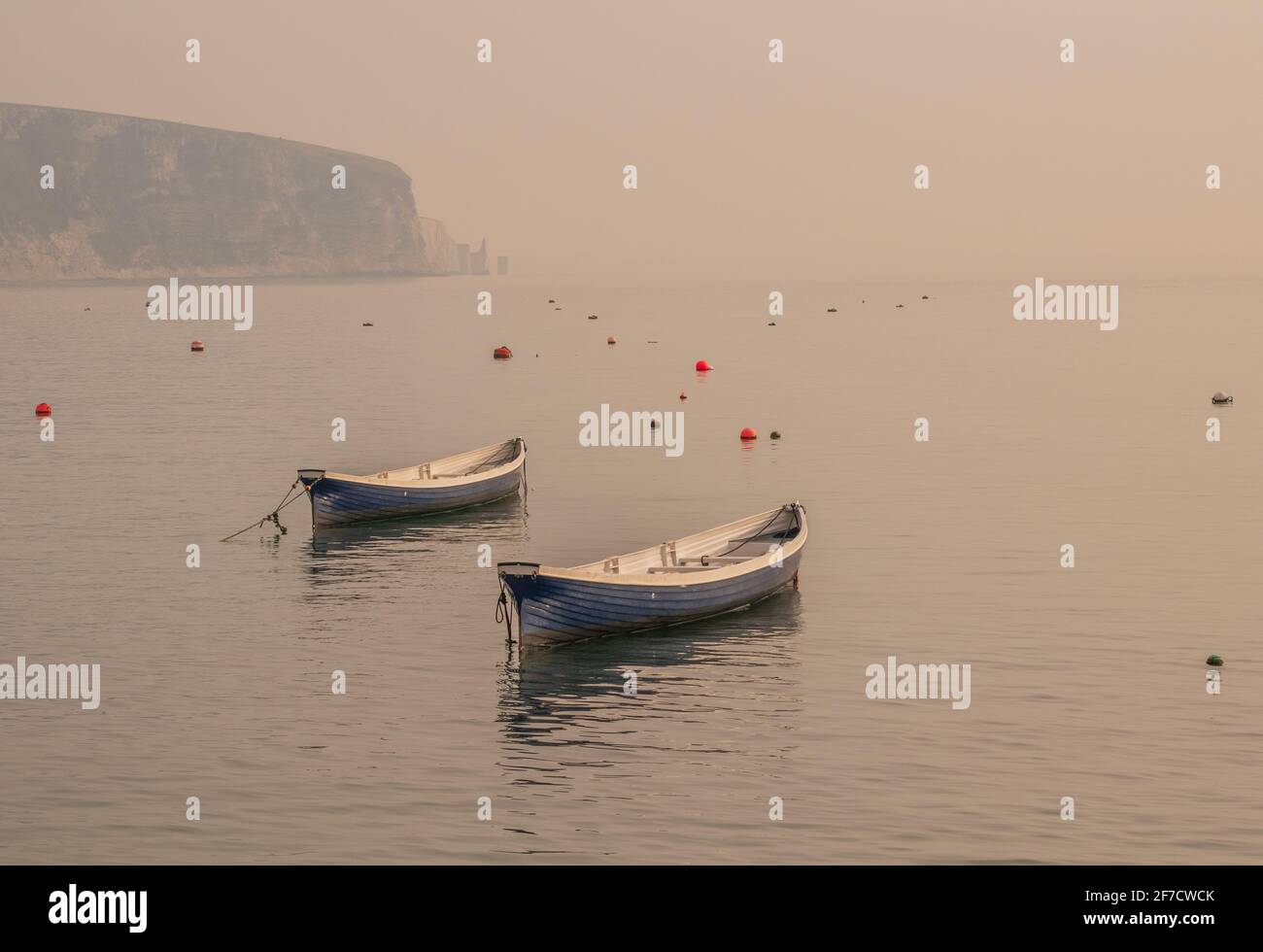 Two empty blue row boats reflect in a still, foggy,misty Dorset ...