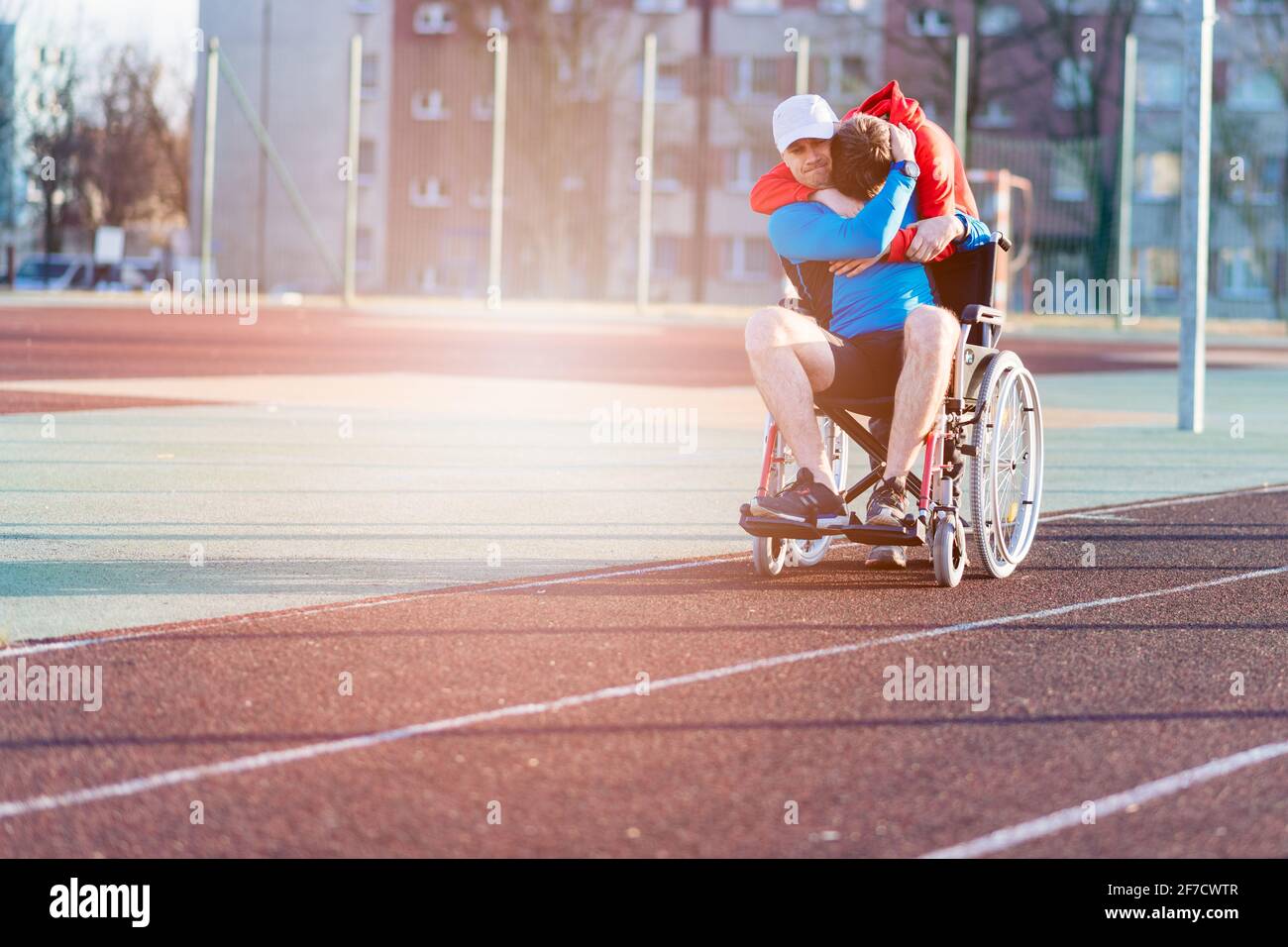 Disabled athlete in a wheelchair on an athletics track. Son hugs his ...