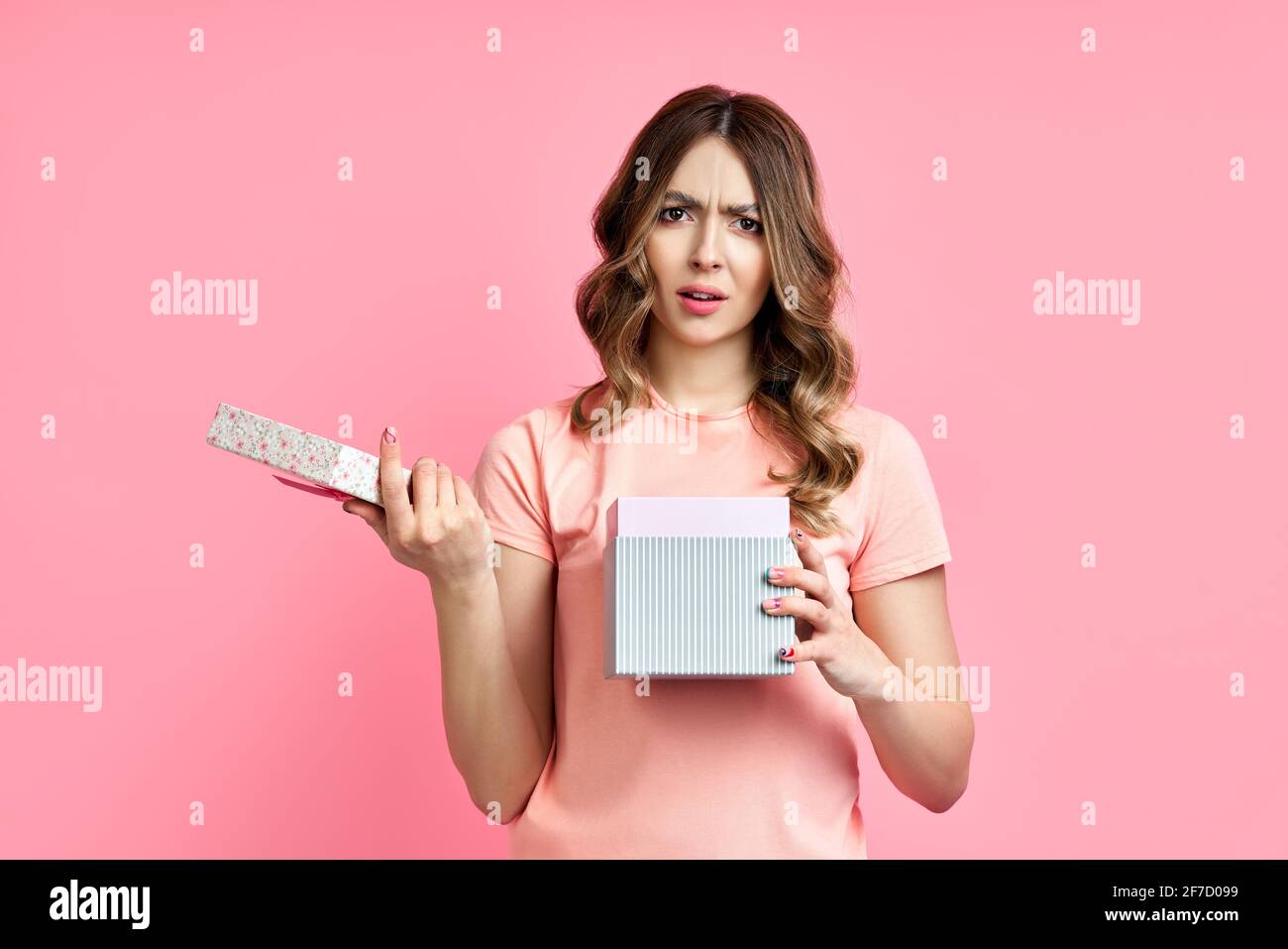 Young woman disappointed with her gift box on pink background. Bad ...