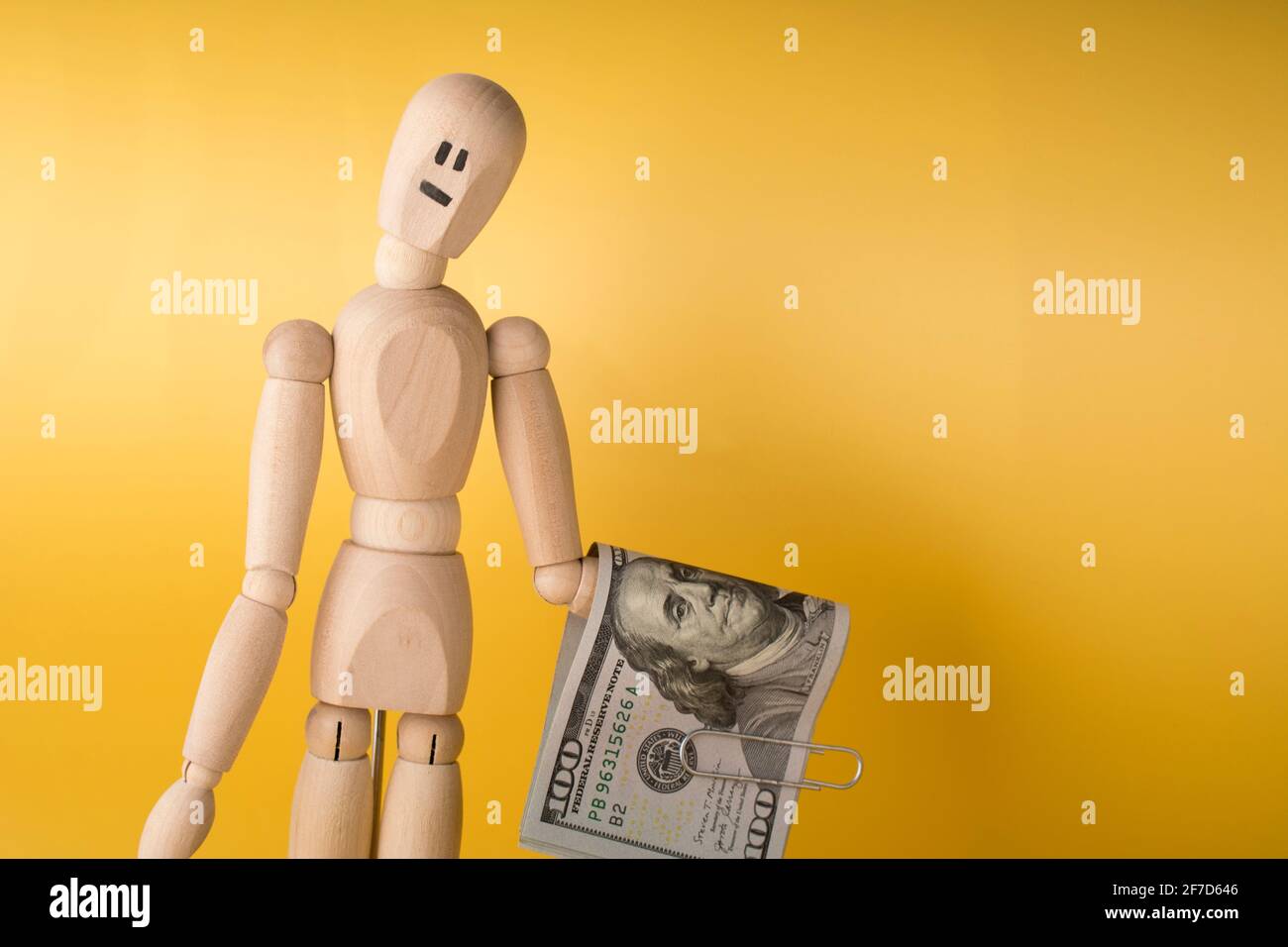 Figure of wooden man with sad expression holds 100 dollar bills with ...
