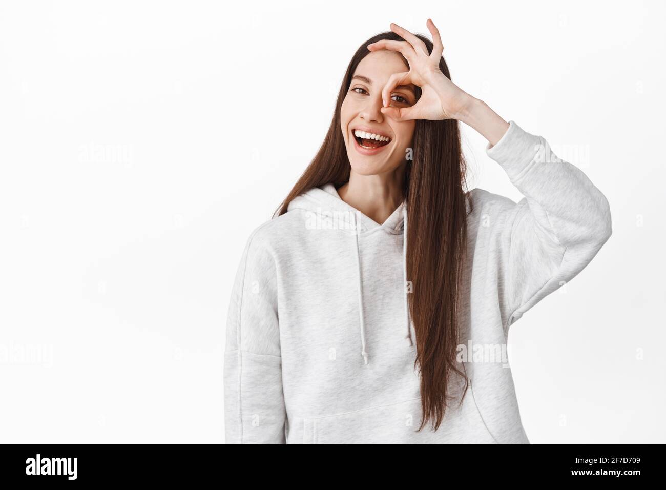 Positive young woman say yes, shows okay sign on eye and smiling, make ...