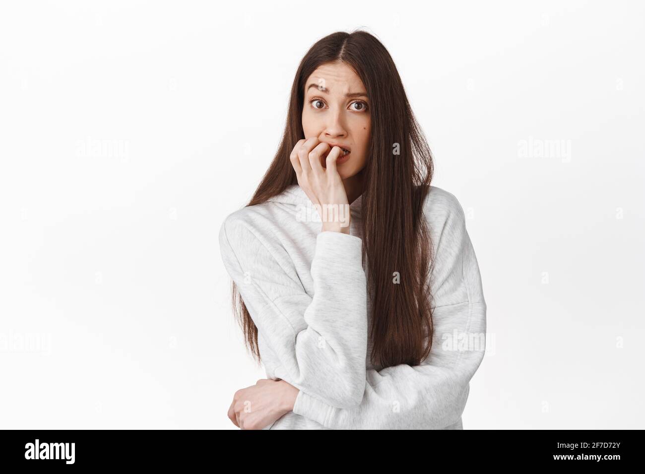 Worried young woman biting fingers and looking at camera, have anxiety ...