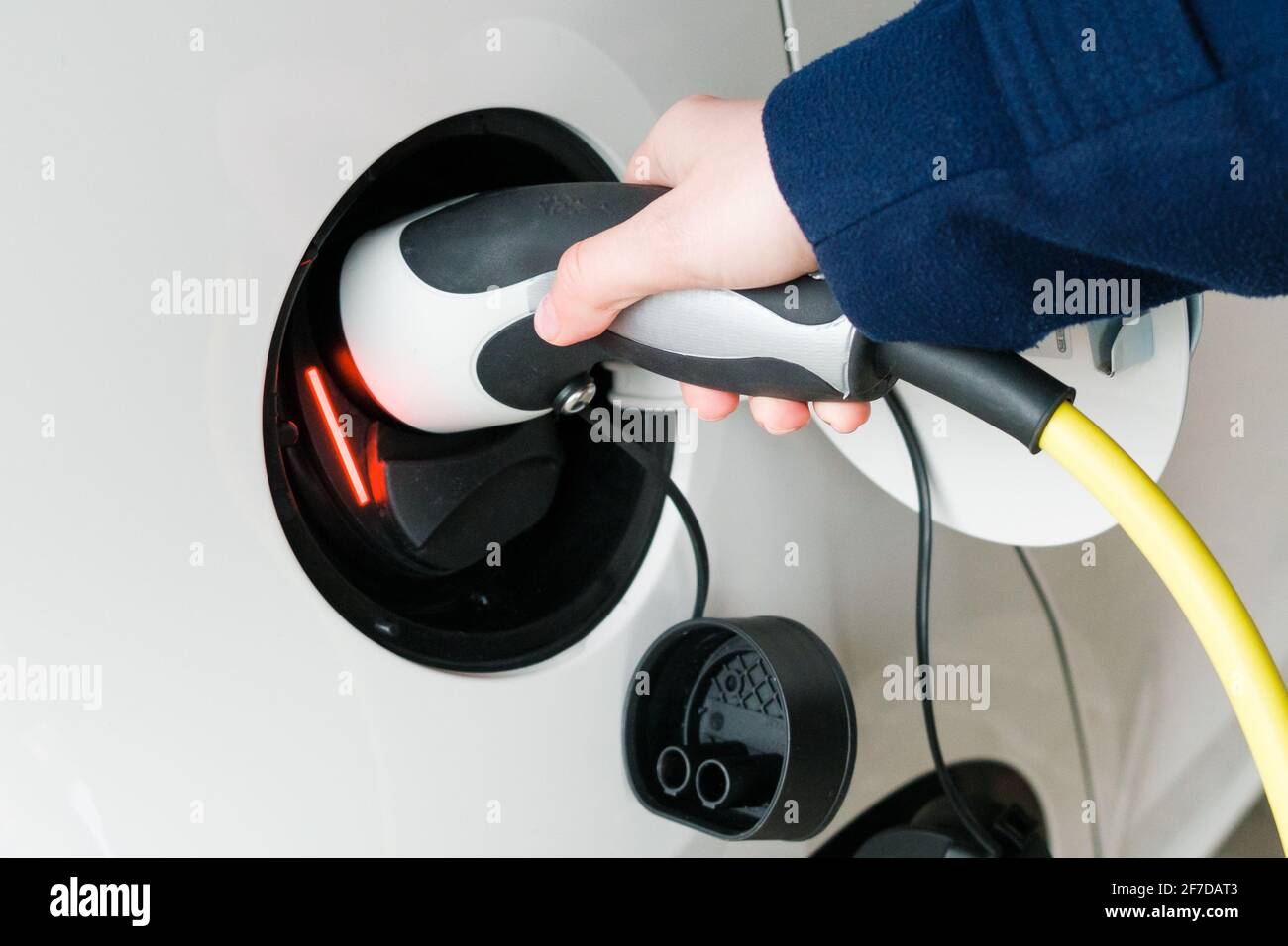 Woman inserts the power supply cable into an electric car for charging ...