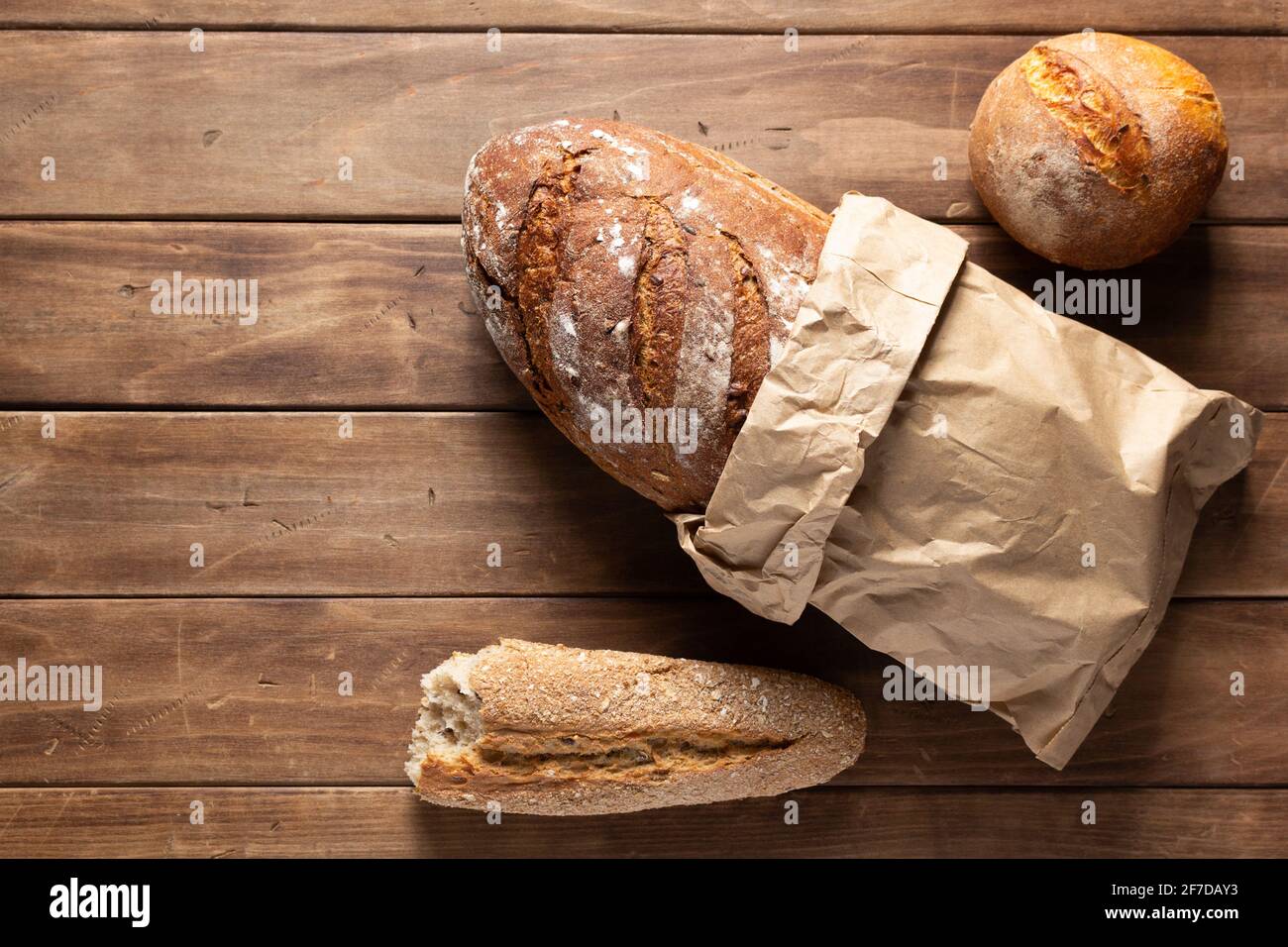 Loaf of fresh bread and buns on wooden table. Assortment of bakery food ...