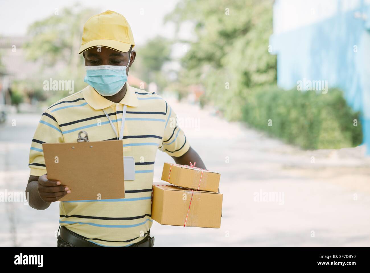 African delivery man holding boxs and cardboard with wearing face mask ...
