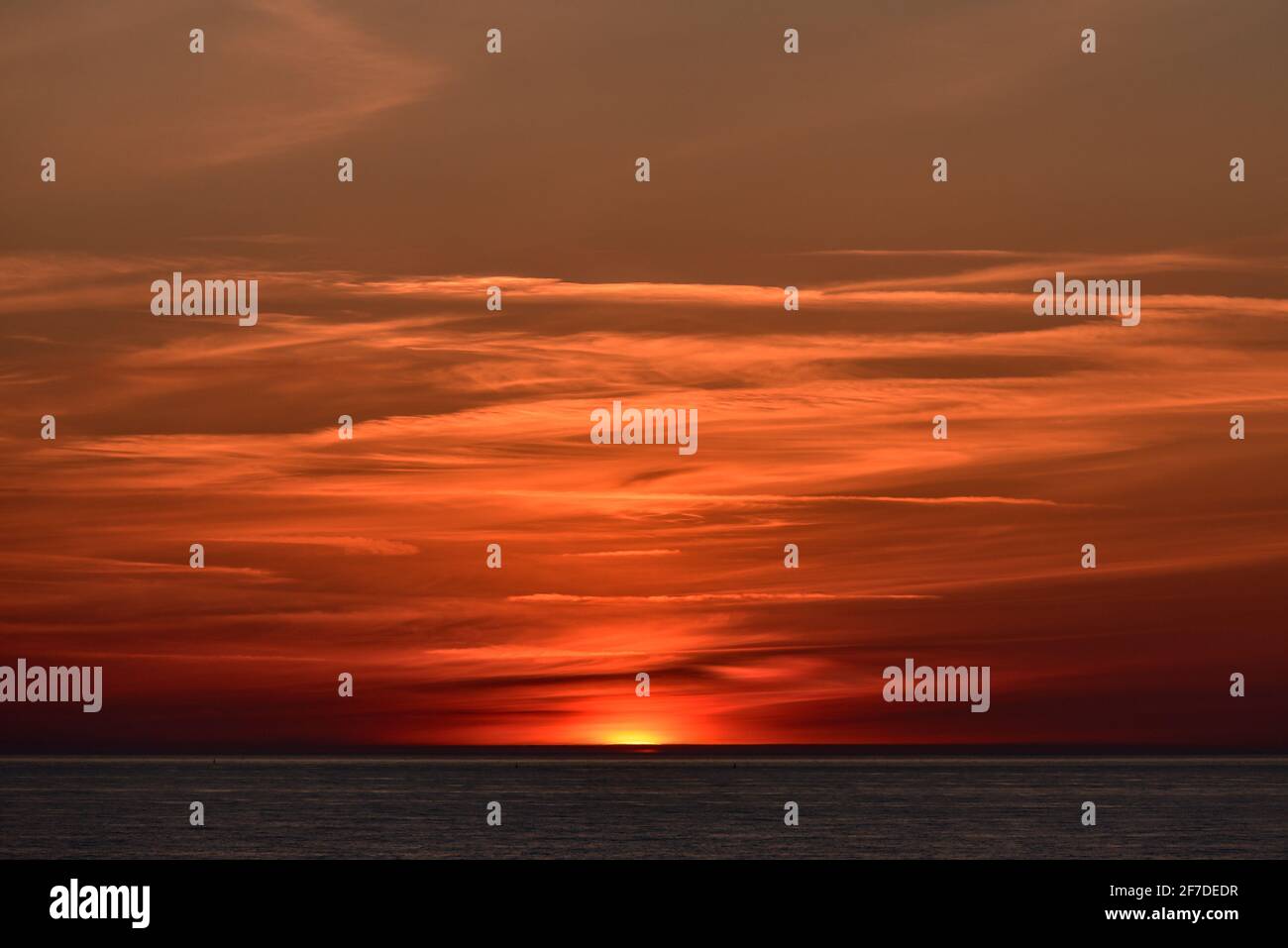 sunset at sea with a calm water surface and a beautifully lit sky ...