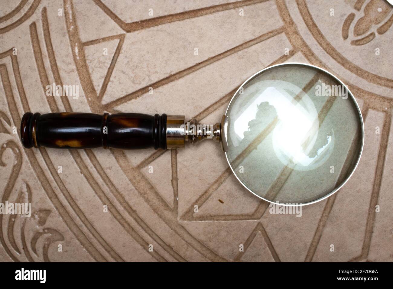 Vintage magnifying glass on intricate beige tile Stock Photo - Alamy