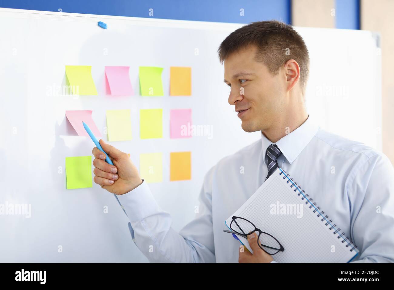 Portrait of male person pointing pen on colorful notes on marker board ...