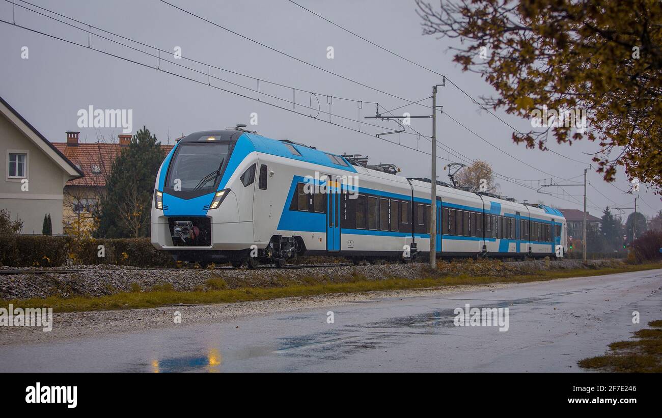 Modern white and blue passenger commuter train passing by in rain ...