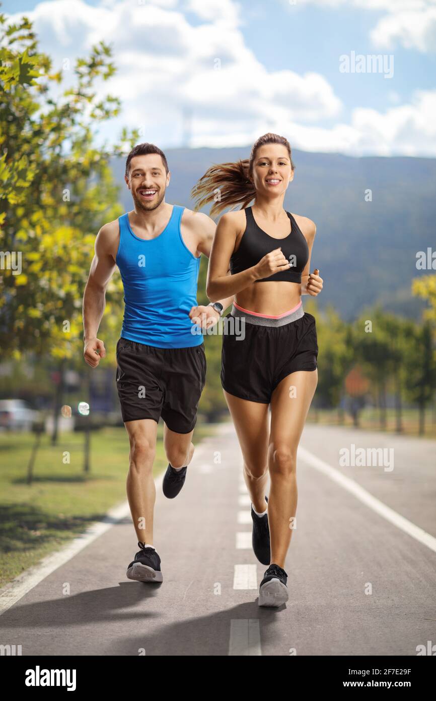 Full length portrait of young man and woman jogging on a running ...