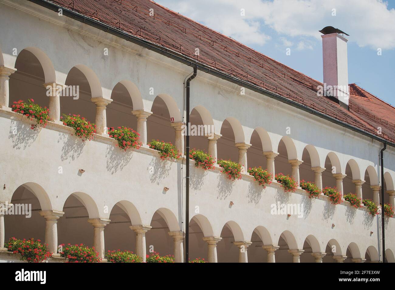 Arched walkway with flowers on the balcony, visible white front facade ...