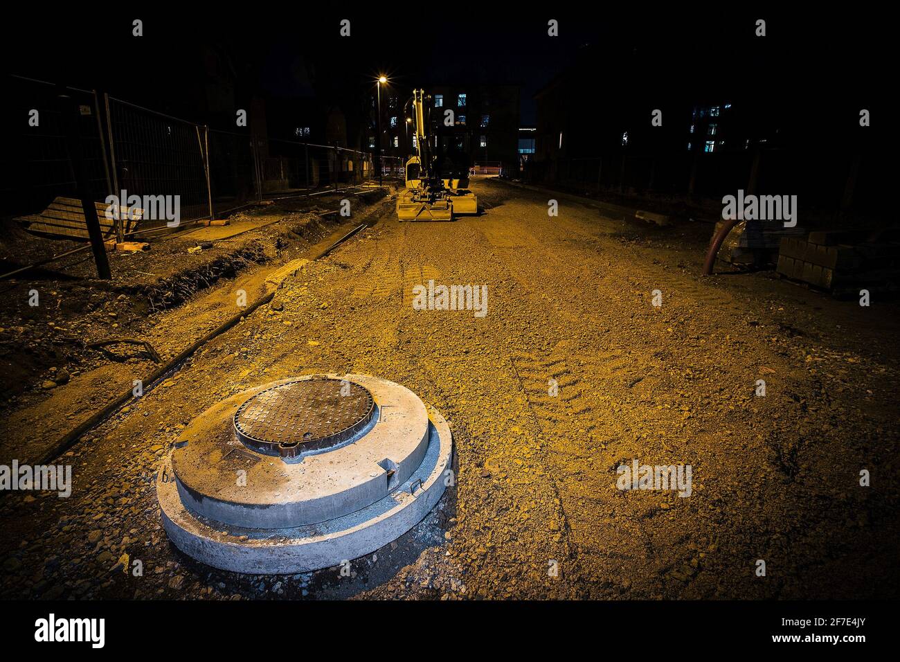 Metal manhole on a city street during the night. An excavator is seen ...