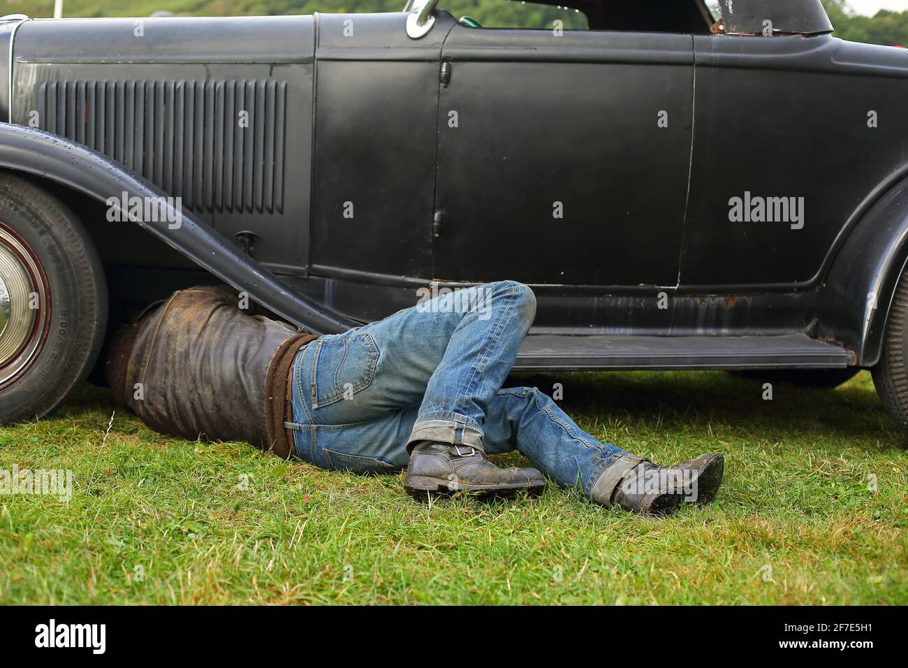 Man wearing a leather jacket and jeans working on the underside of a ...