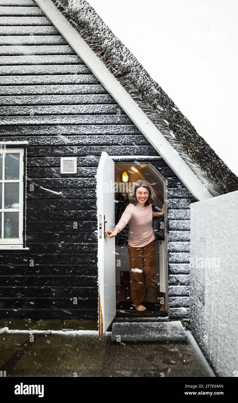 Smiling Woman in Mid-50s Opening Door During a Snow Storm in Denmark ...