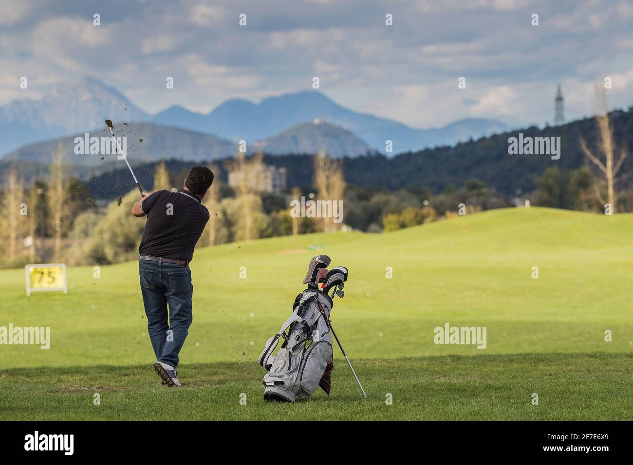 a man hitting a golf ball on a driving range of a golf field. Visible ...