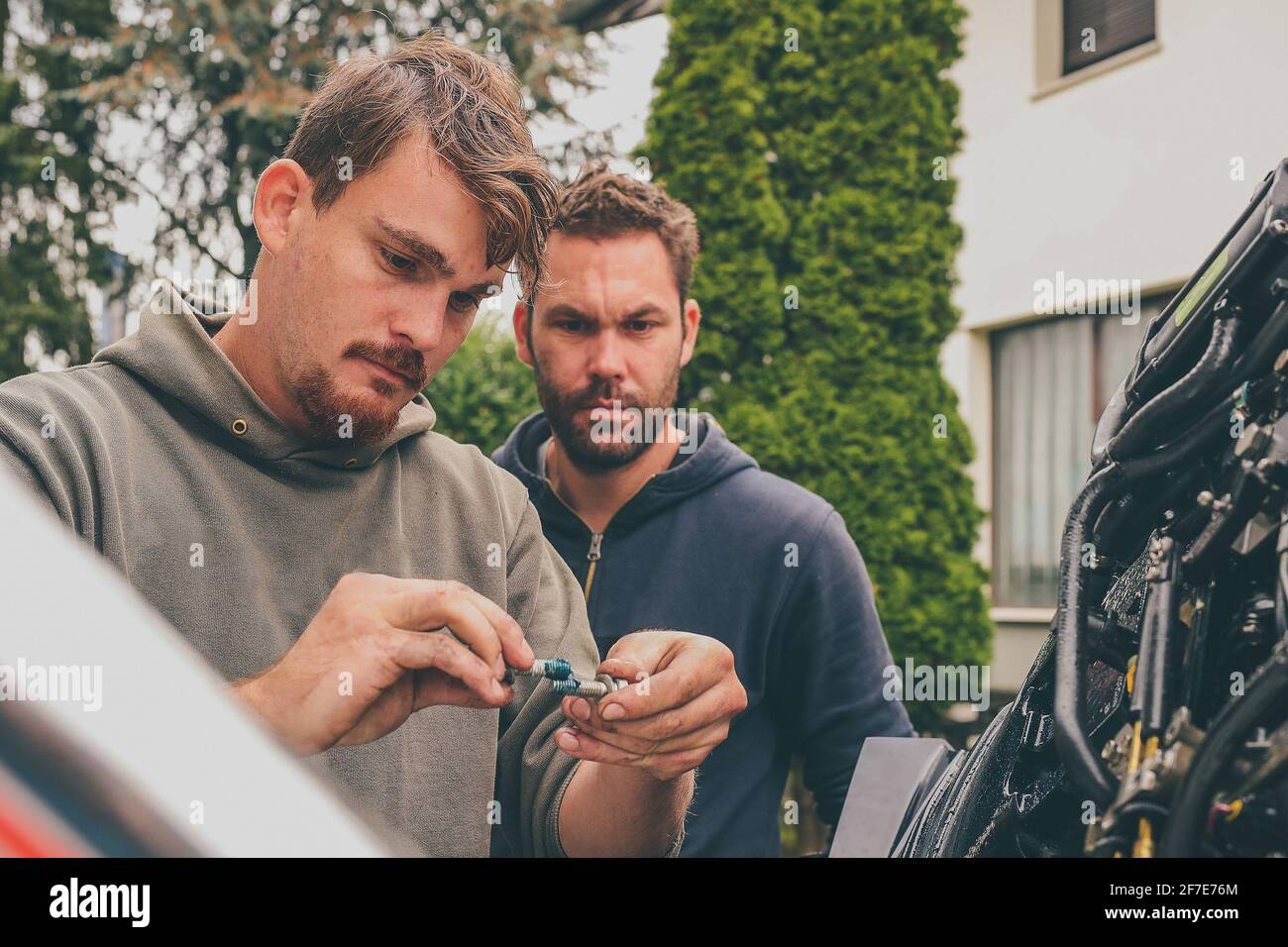 Two people greasing two metal screws with blue grease in order to ...