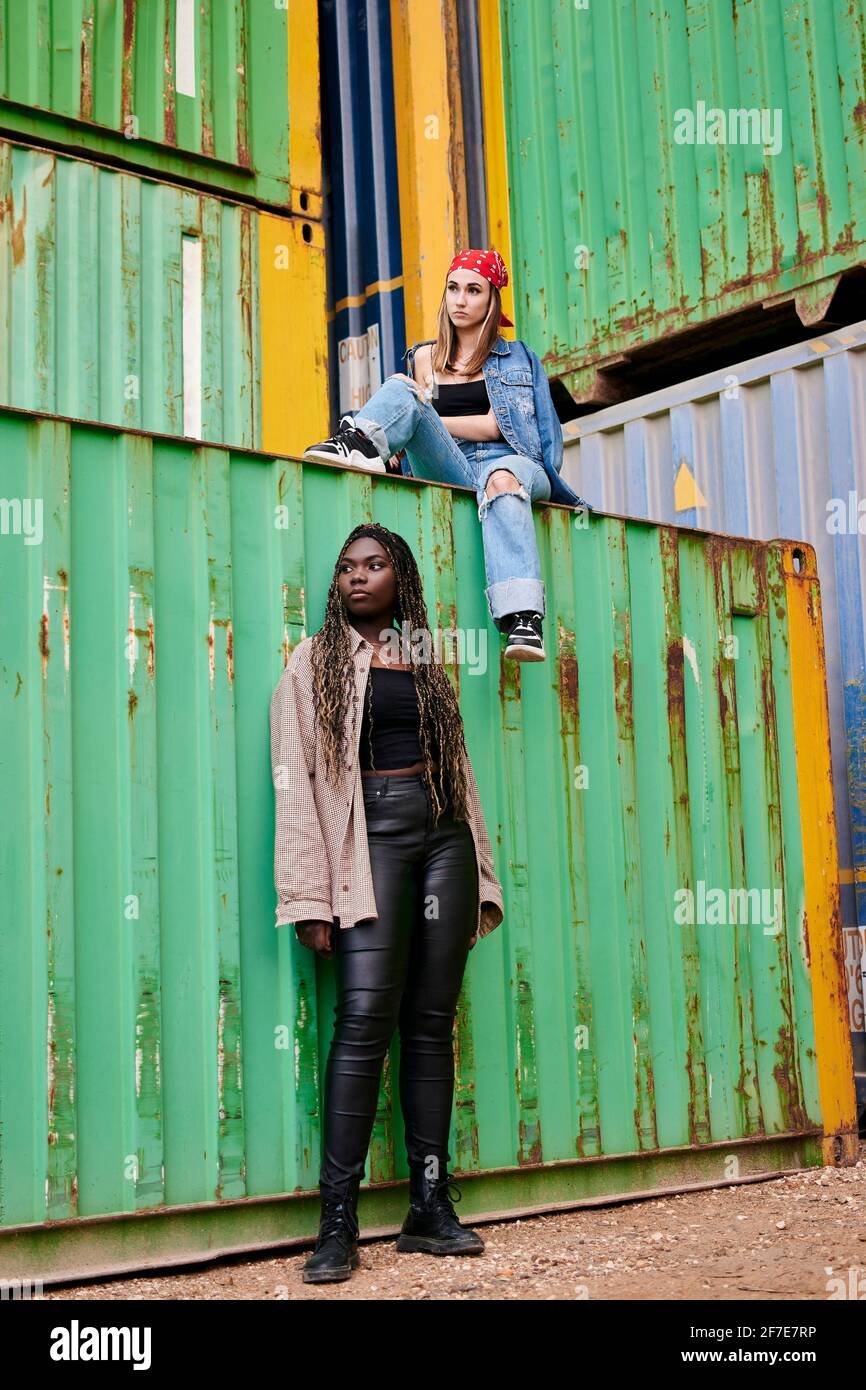 Two women wearing urban clothing surrounded by shipping containers ...