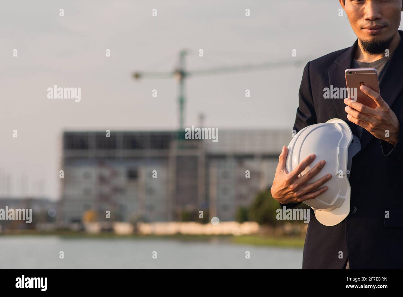 Asian businessman call cellphone hold white hard hat looking on screen ...