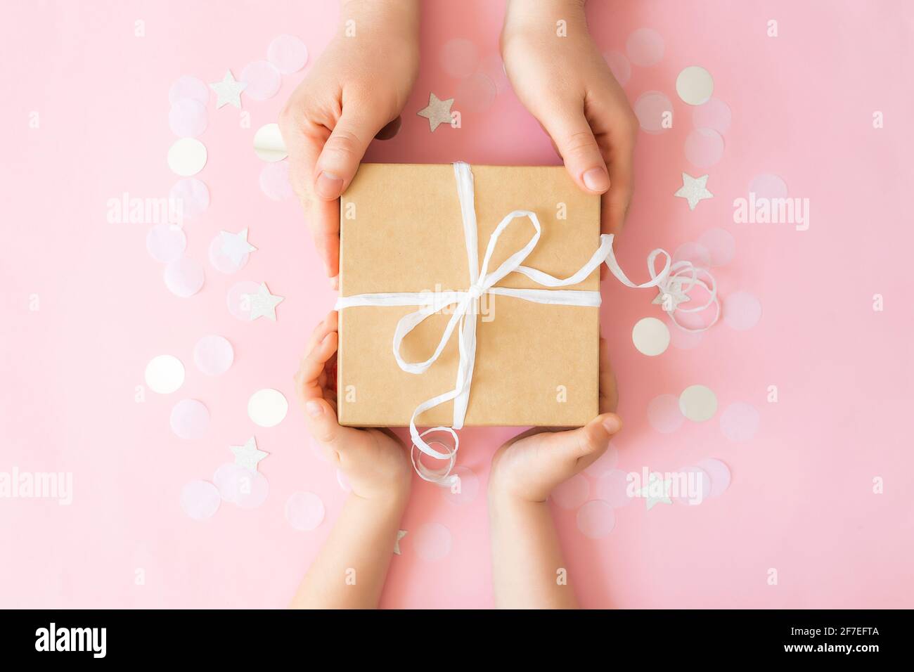 Flat lay with isolated hands giving a craft paper gift box tied with ...