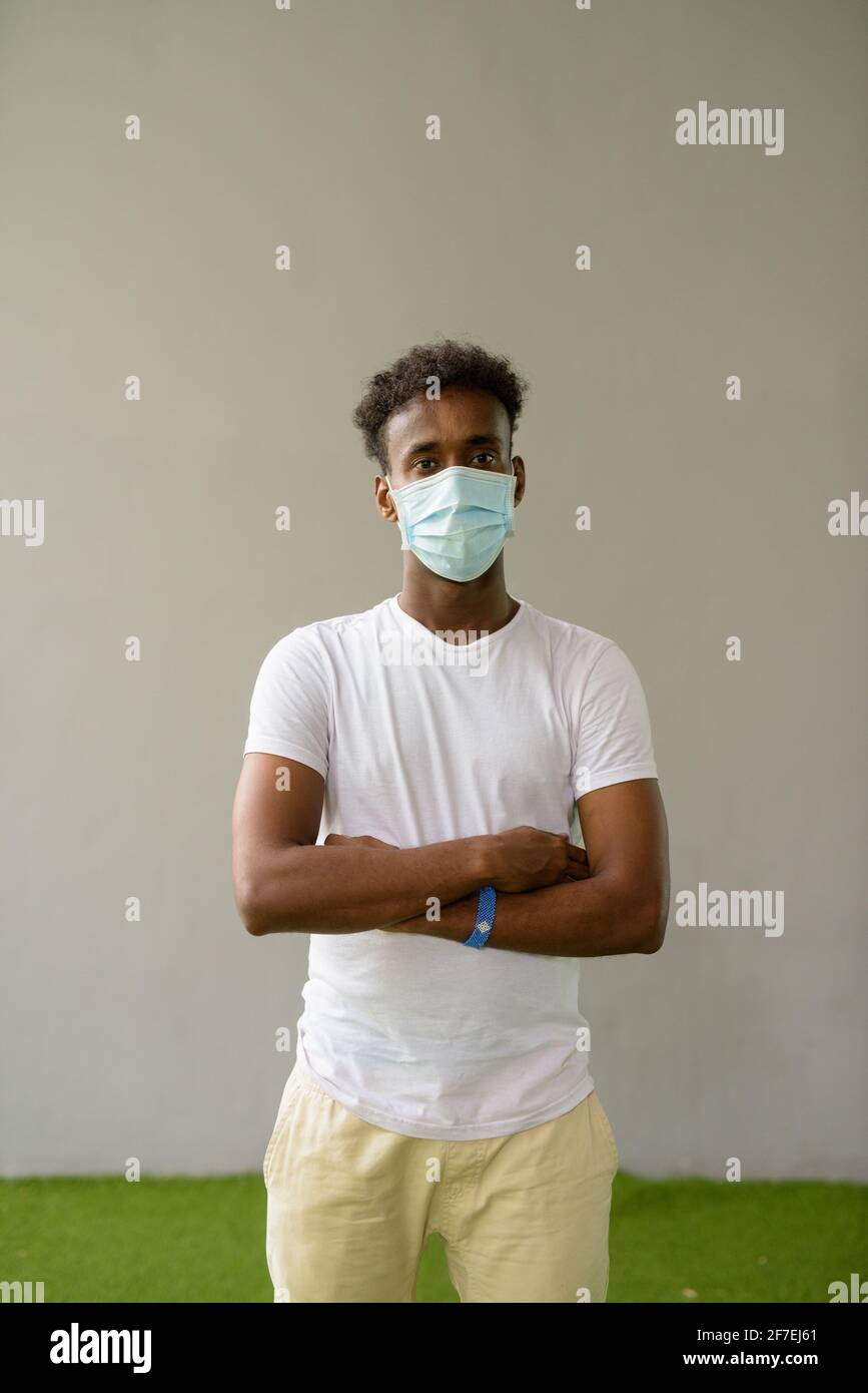 African man wearing face mask against plain wall background with arms ...