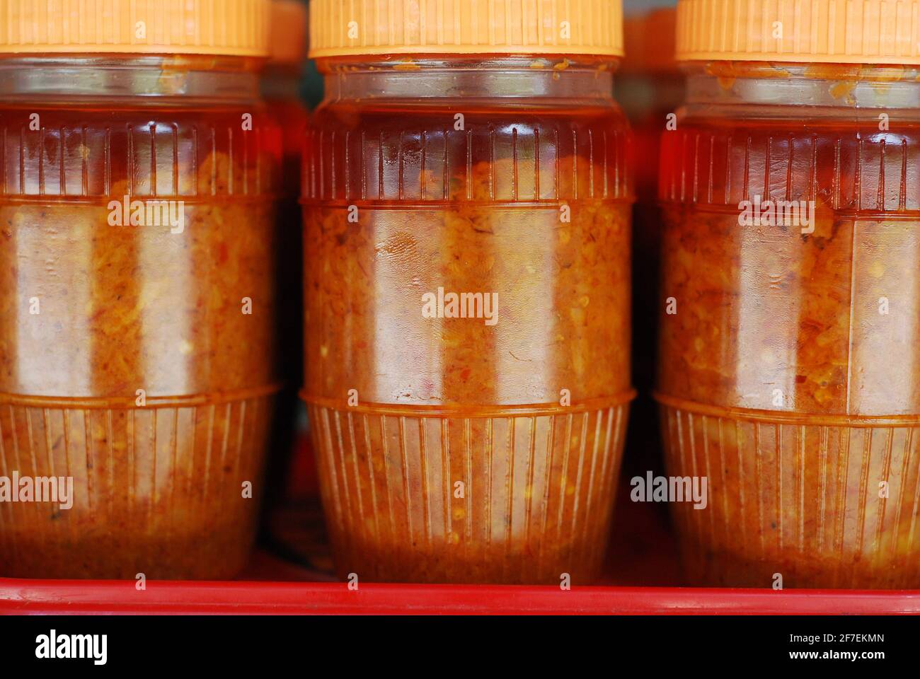 Small plastic jars full of home-made chilli oil for sale. Image shows ...