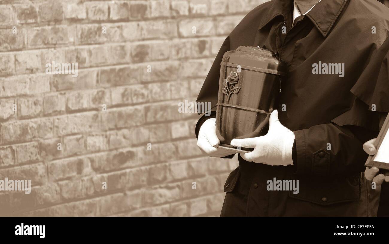 Funeral director or undertaker carrying a smooth metal urn in his hands ...