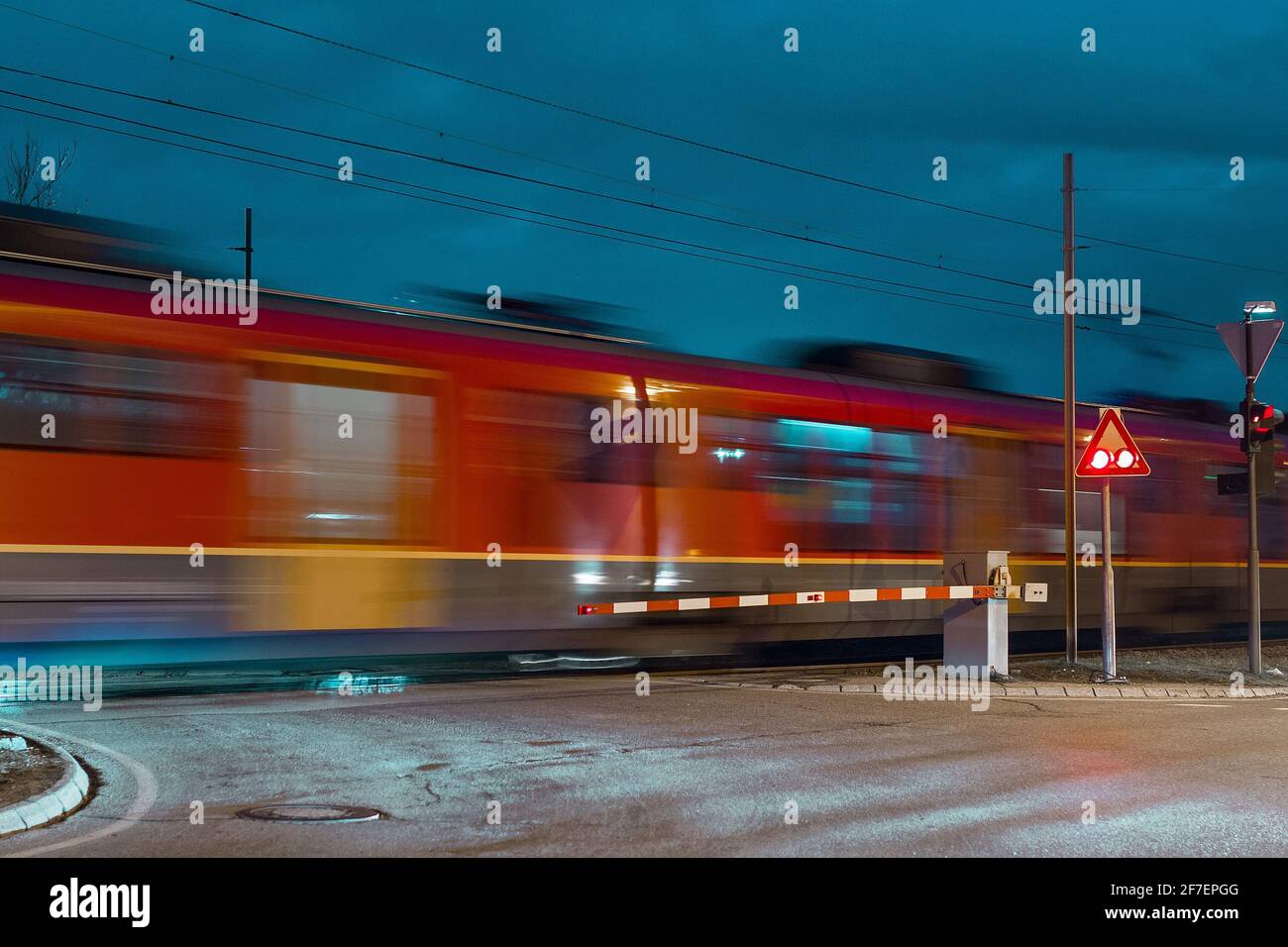 Fast moving red train passing grade crossing with barriers down and red ...