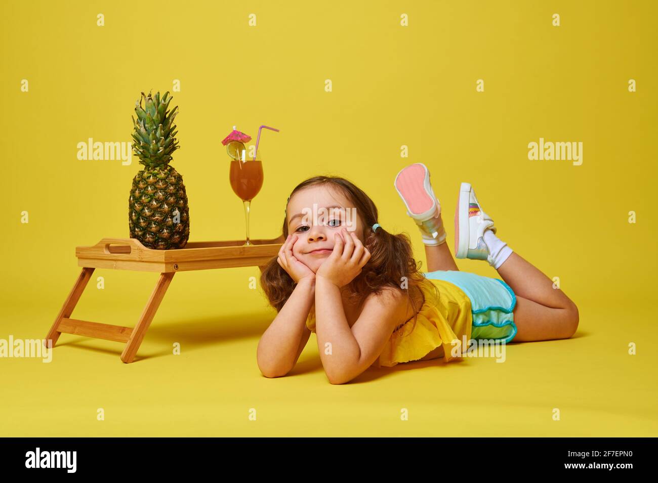 Beautiful little girl wearing summer clothes lying on yellow background ...