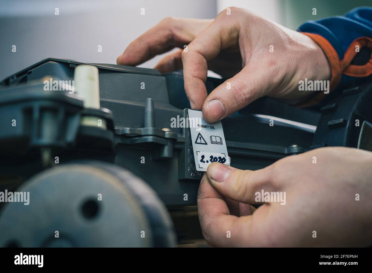 Applying a new warranty seal sticker on a robotic lawnmower after a ...