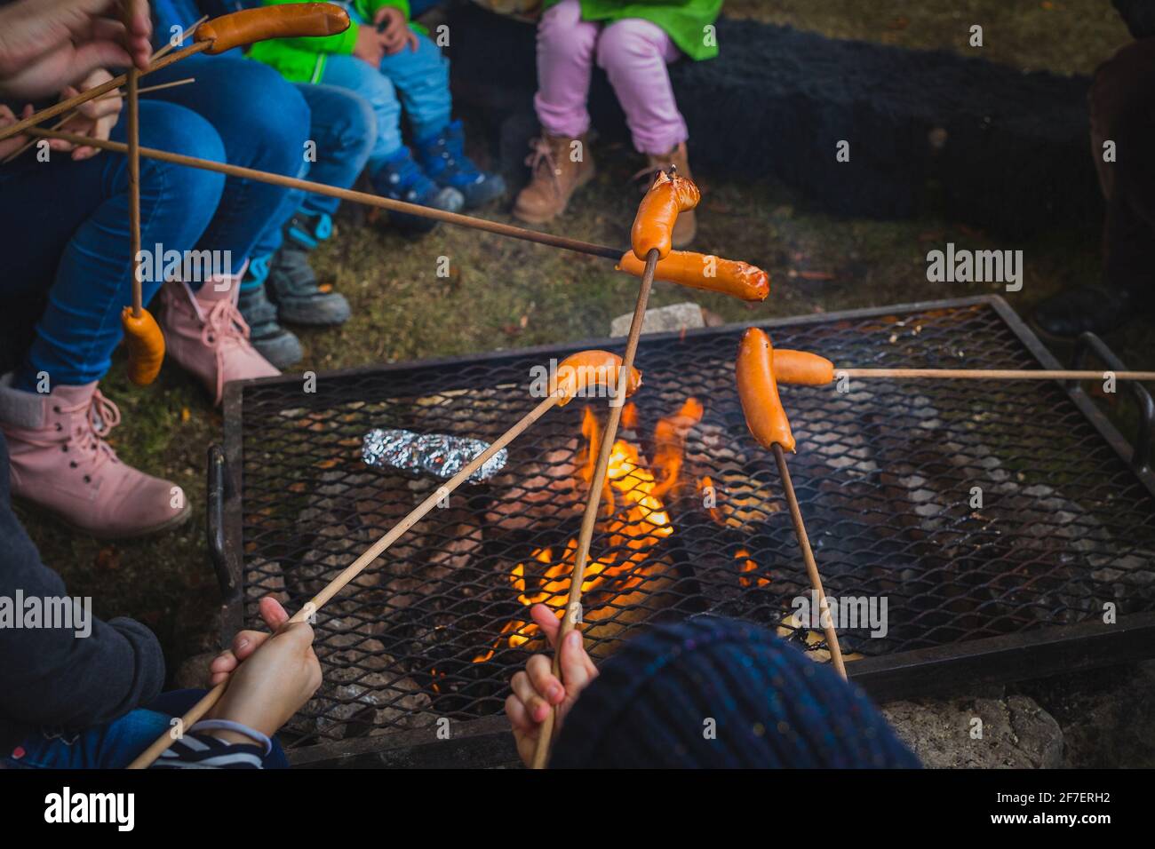 Hands od kids with sticks and sausages are seen holding over a charcoal ...