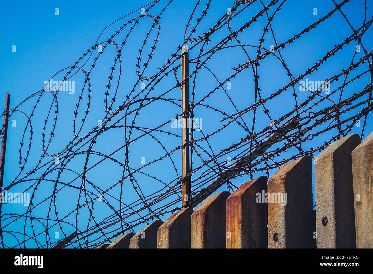 Sharp barbed wire on a top of a concrete wall in front of a blue sky in ...